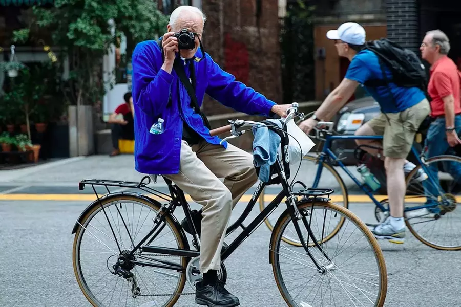 Bill Cunningham en blua jako sur biciklo