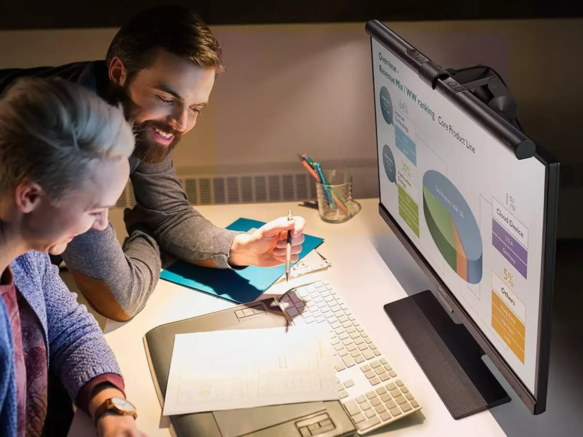 hombre y mujer sonrientes sentados frente a la computadora con la lámpara de tareas LED de lectura electrónica BenQ ScreenBar