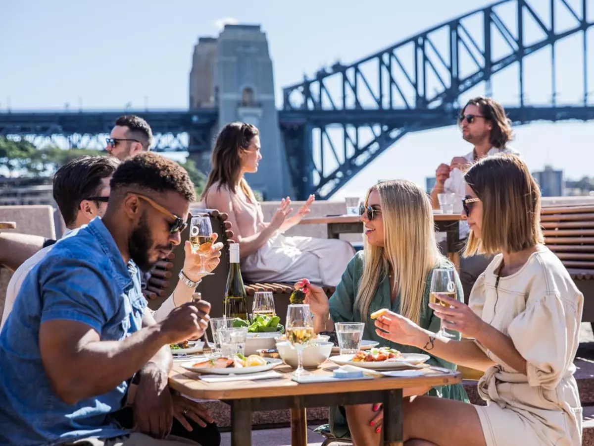 grupa ljudi jede u opernom baru ispred lučkog mosta u Sydneyju