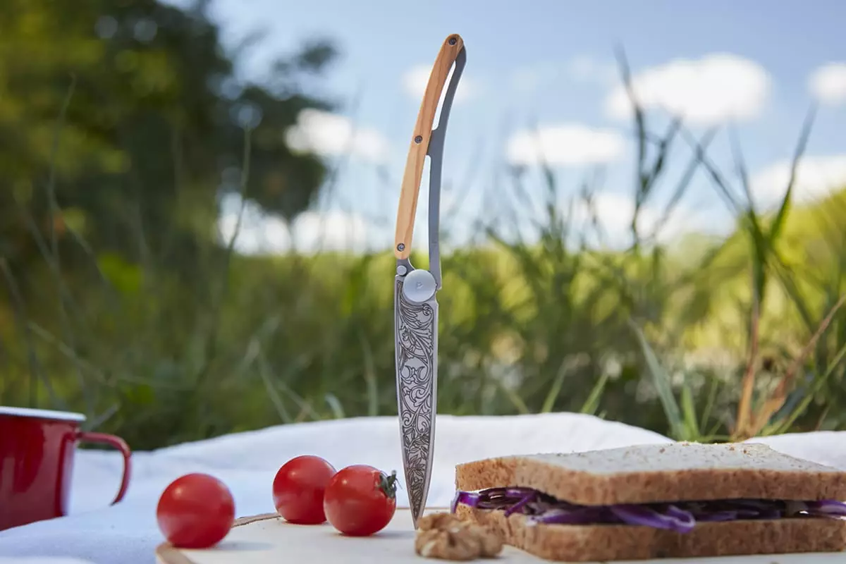 Ένα μαχαίρι Deejo με ξύλινη λαβή μαχαιρωμένο σε ένα τραπέζι για να στέκεται όρθιο